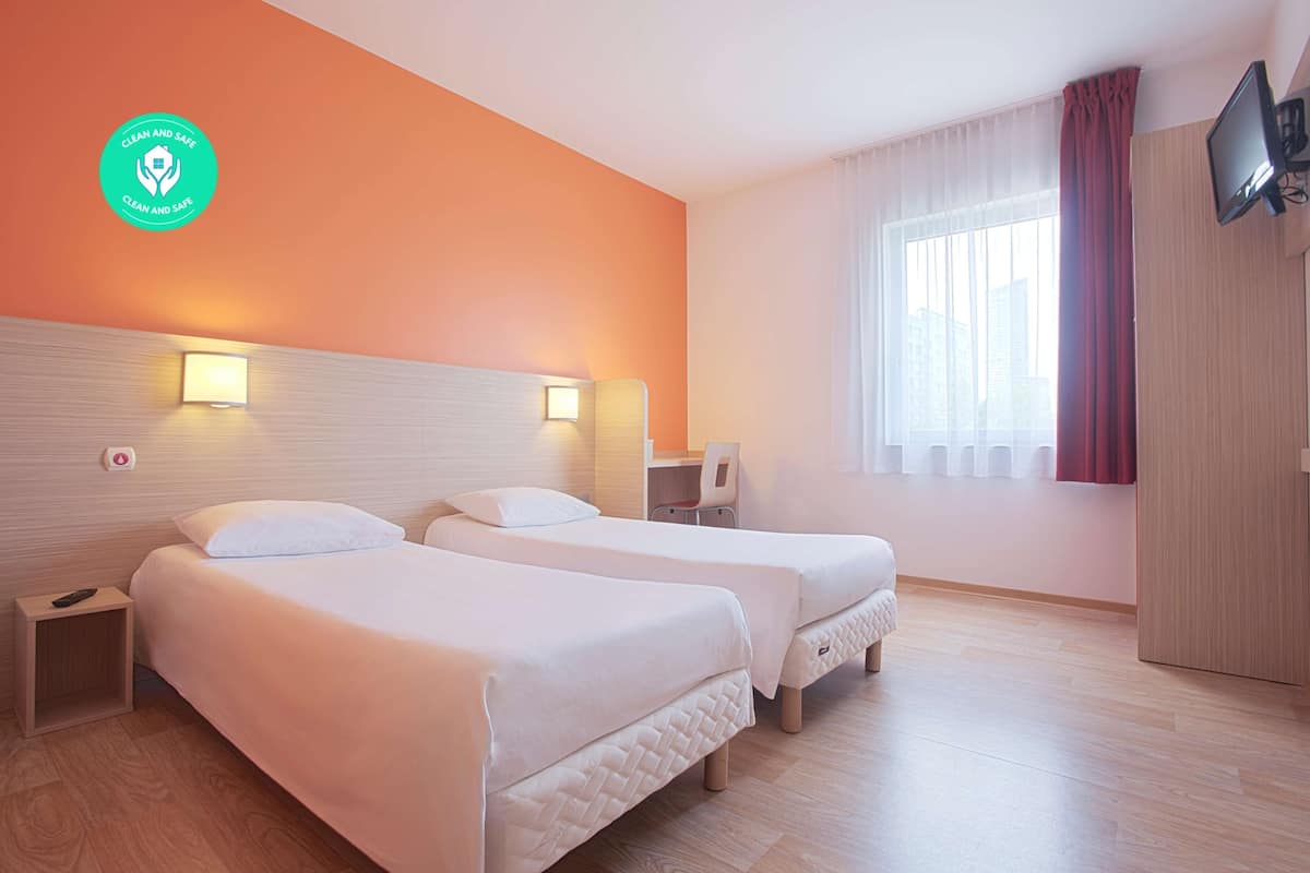 Quarto de hotel com duas camas, televisão, escrivaninha e janela com cortinas.