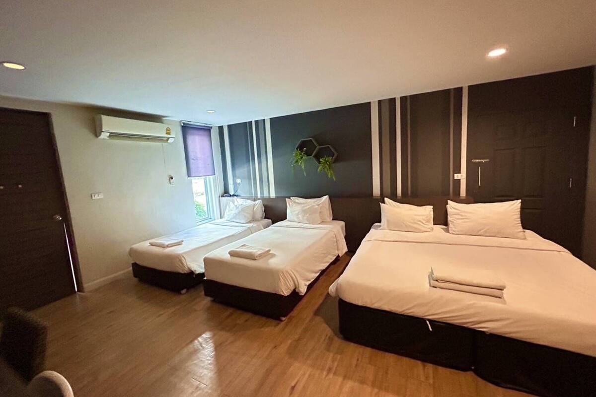 Quarto de hotel moderno com duas camas de solteiro e uma cama de casal, piso de madeira e janela com persianas.