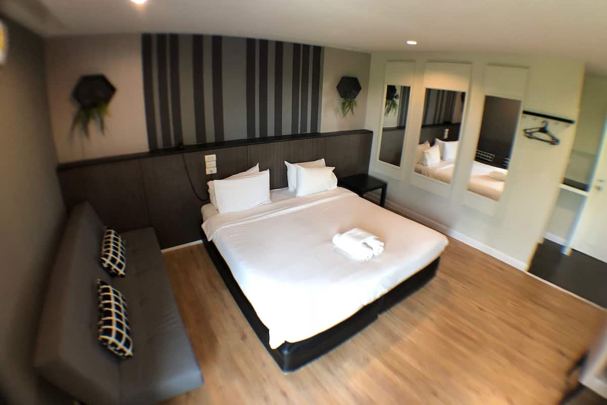 Quarto de hotel moderno com uma cama grande, mesa de cabeceira, sofá e espelho.