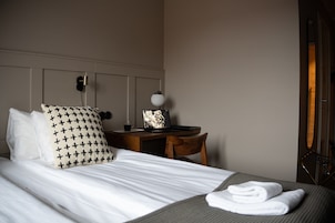 Quarto de hotel com cama, escrivaninha com luminária, cadeira e telefone fixado na parede.
