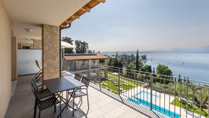 Varanda com mesa e cadeiras, um pilar de pedra e vista para uma piscina e mar.