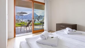 Quarto de hotel com uma cama, uma mesa de cabeceira de madeira e vista para uma piscina e montanhas.