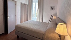 Quarto com cama, luminária de cabeceira, guarda-roupa e janela com cortinas.