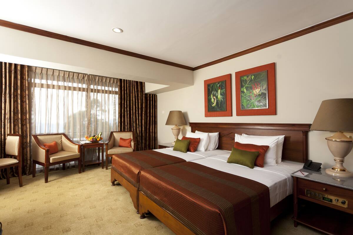 Quarto de hotel com uma cama grande, duas mesas de cabeceira, uma escrivaninha, uma cadeira e uma janela com cortinas.