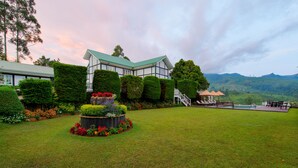 Um edifício grande e tradicional com telhado verde, rodeado por jardins bem cuidados e área de piscina.