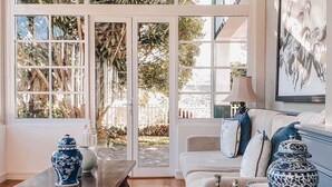 Um quarto iluminado pelo sol, com uma janela grande, um sofá, uma mesa de centro e vasos decorativos.