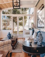 Um quarto iluminado pelo sol, com uma janela grande, um sofá, uma mesa de centro e vasos decorativos.
