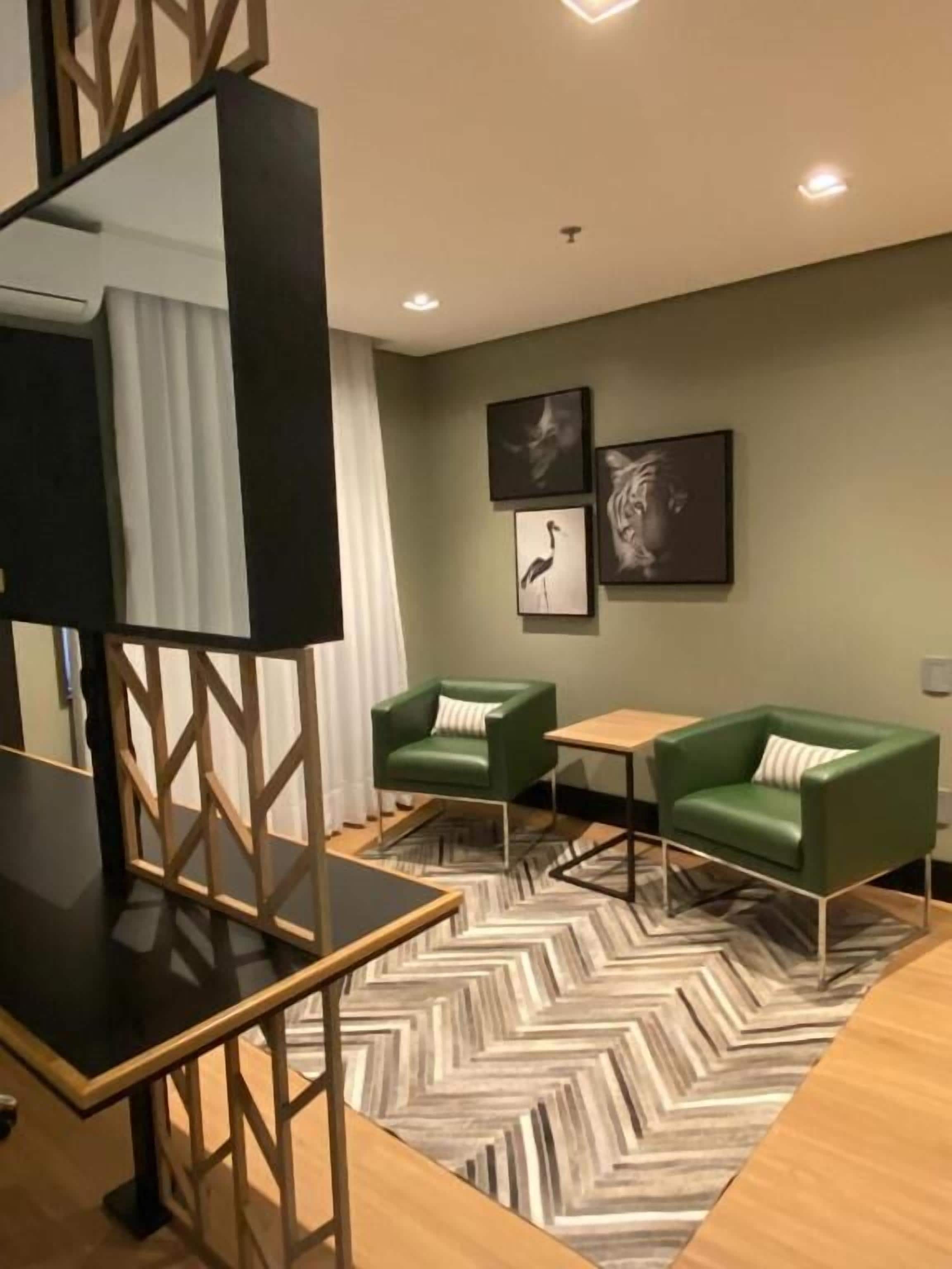 Quarto moderno com dois sofás de couro verde, uma mesa de madeira pequena e um tapete estampado.