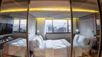 Quarto de hotel moderno com uma cama grande, televisão e vista para a cidade.