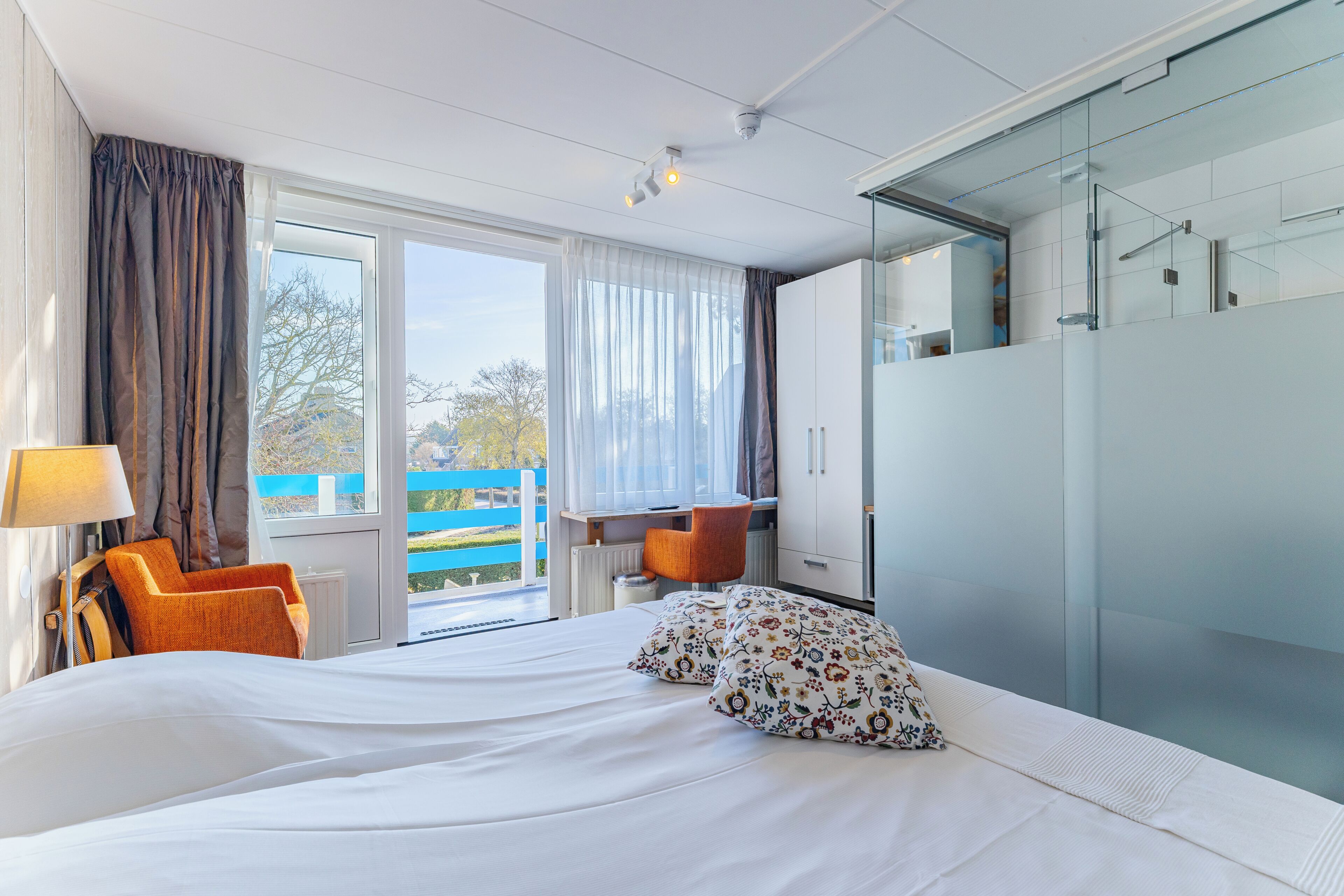 Quarto de hotel com cama, uma cadeira, escrivaninha, guarda-roupa e vista para o exterior.