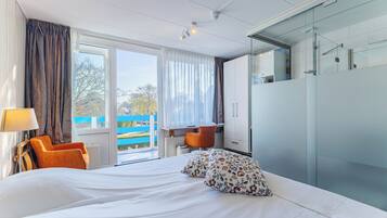 Quarto de hotel com cama, uma cadeira, escrivaninha, guarda-roupa e vista para o exterior.