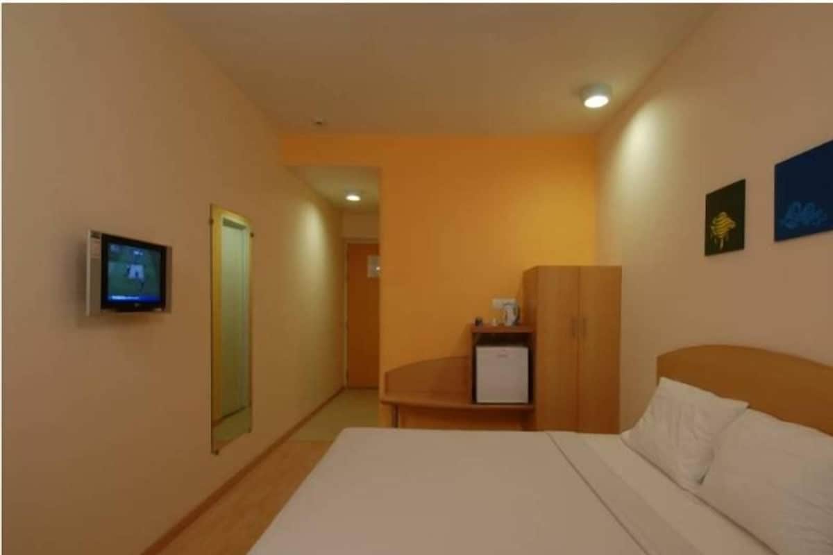 Quarto de hotel com uma cama, televisão, guarda-roupa e uma pequena escrivaninha com um computador.