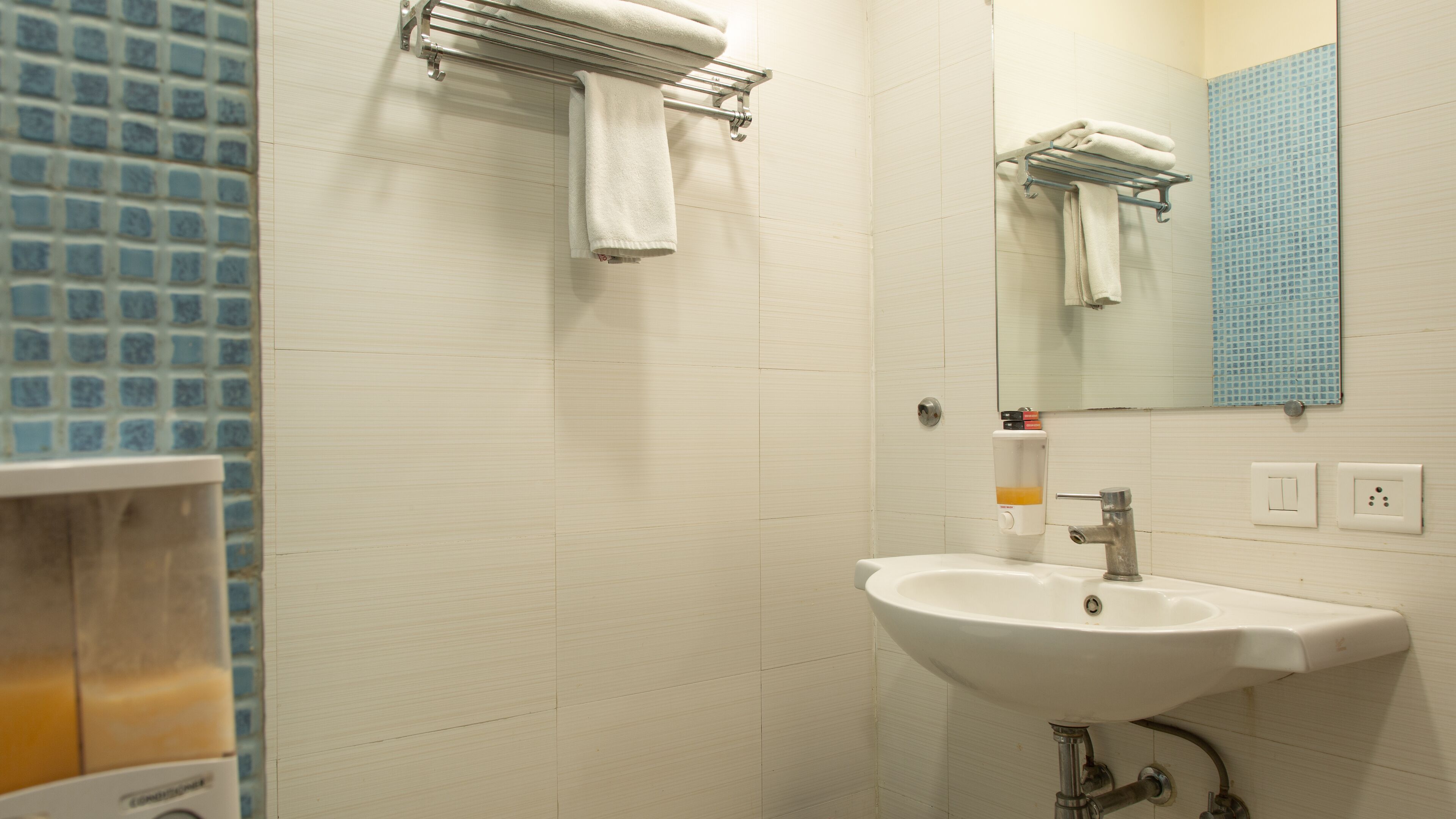 Casa de banho com lavatório branco, espelho e suporte para toalhas.