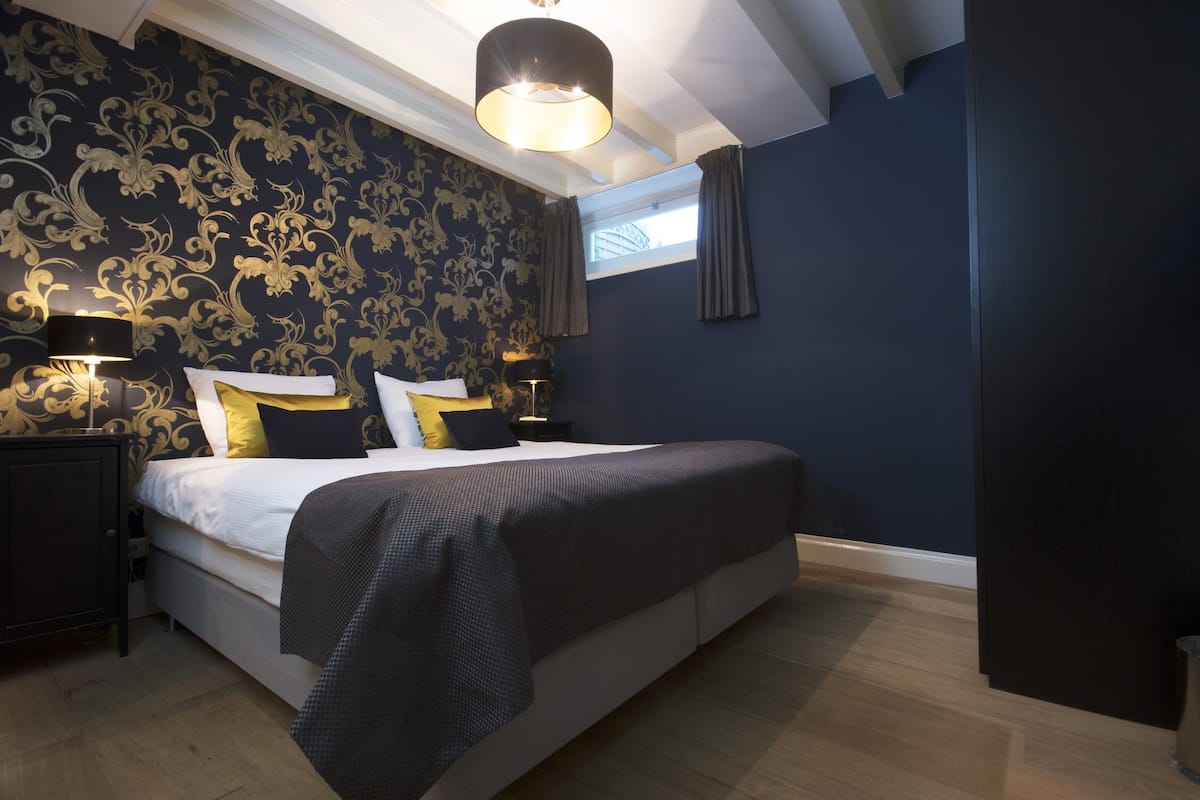 Quarto com cama grande, paredes escuras e papel de parede estampado.