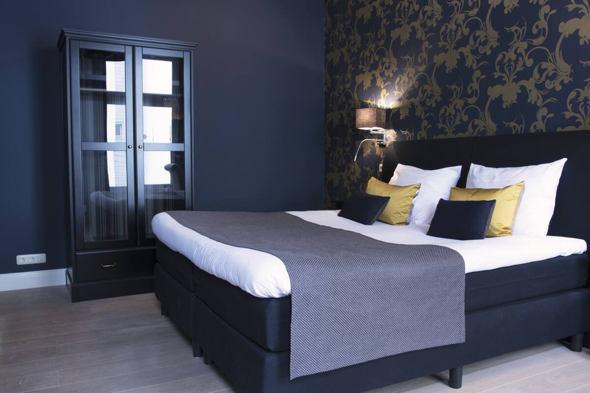 Quarto com uma cama grande, paredes escuras e papel de parede estampado.