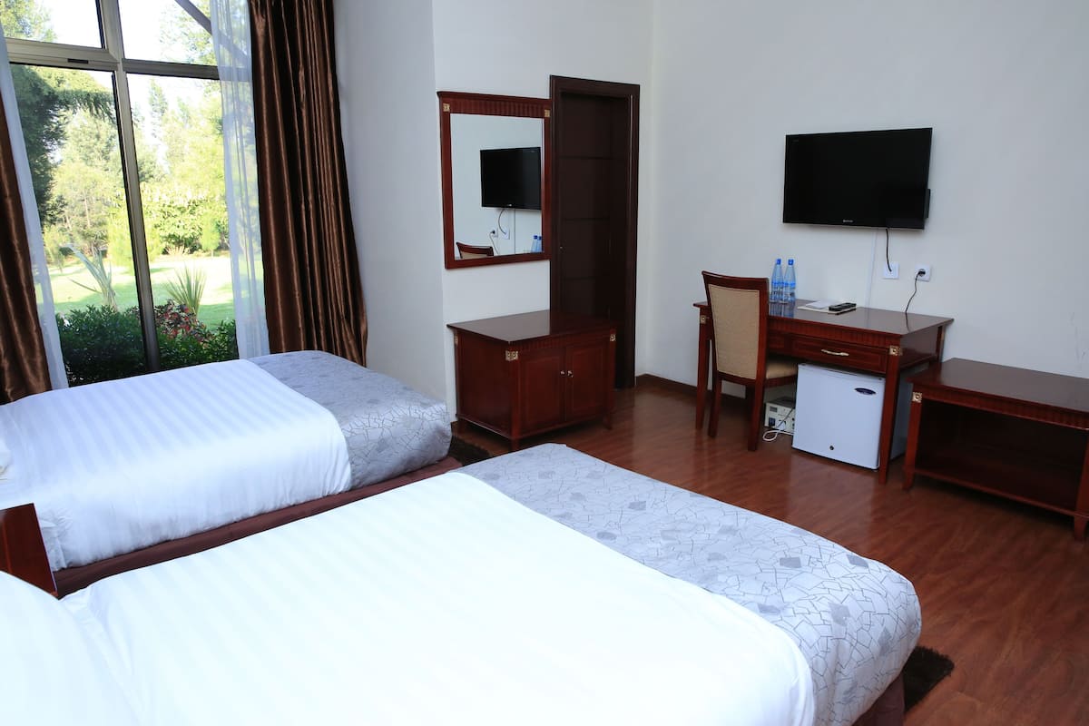 Quarto de hotel com duas camas, uma escrivaninha, televisão e um pequeno frigorífico.