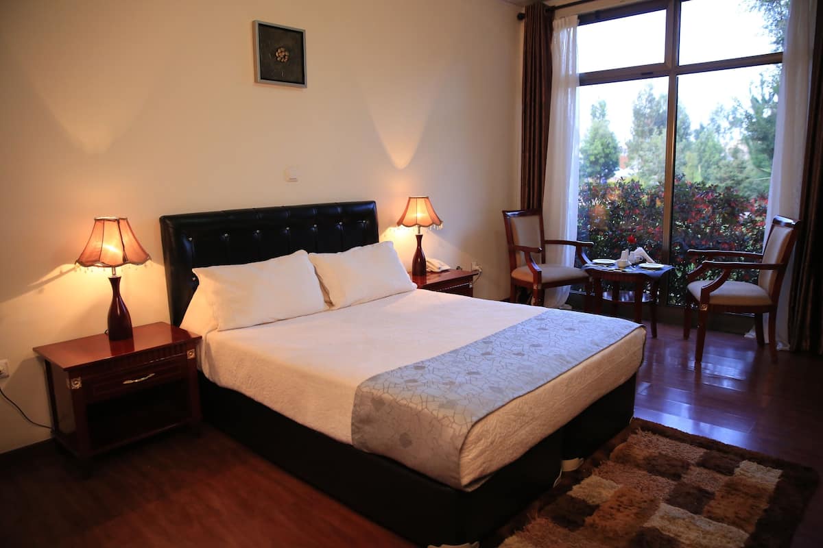 Um quarto com uma cama grande, duas mesas de cabeceira com abajures, uma cadeira e uma vista pela janela.