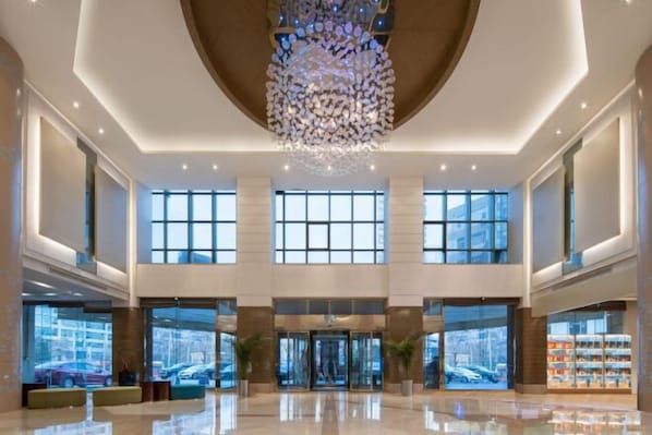 Um hall amplo com teto alto, janelas grandes e um lustre moderno.