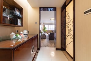 Um hall de hotel com balcão de recepção, área de café e vista para uma sala de estar com sofá e planta.