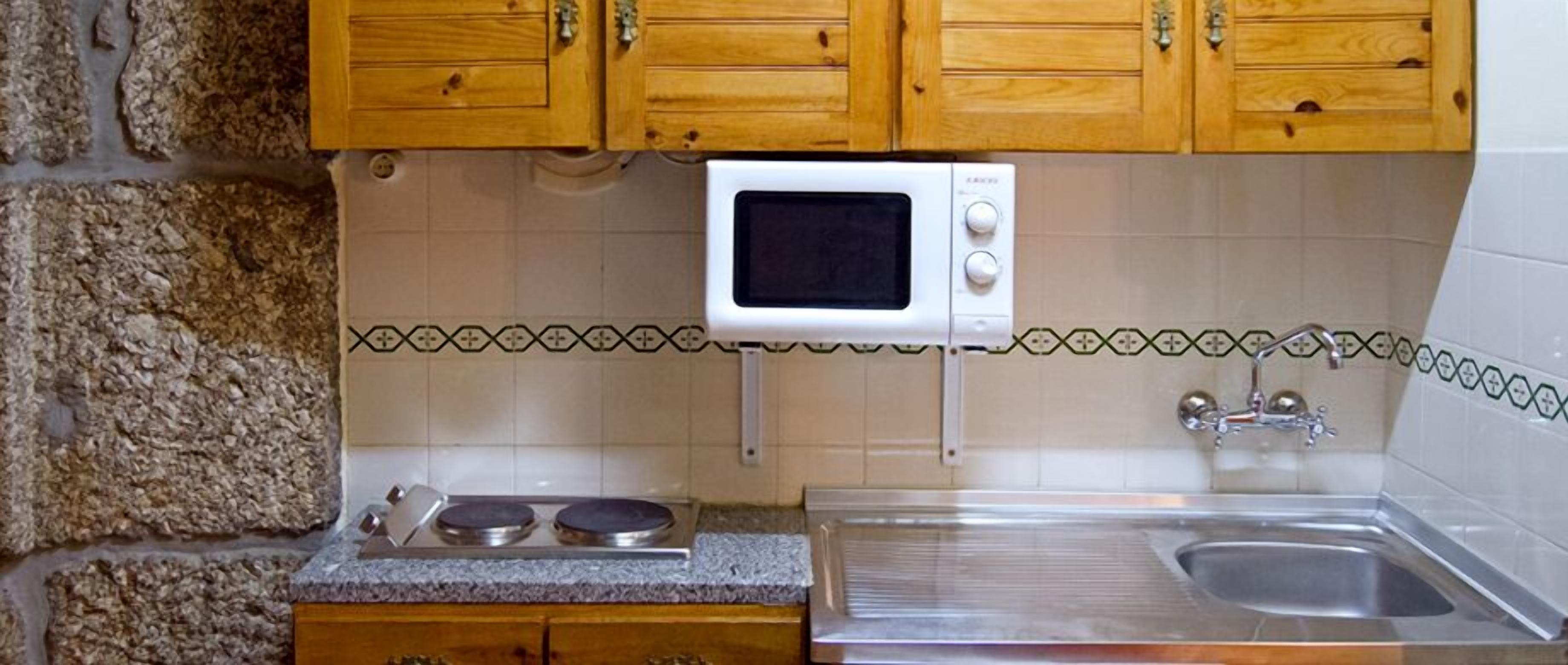 Cozinha com armários de madeira, micro-ondas branco, fogão a gás e pia de aço inoxidável.
