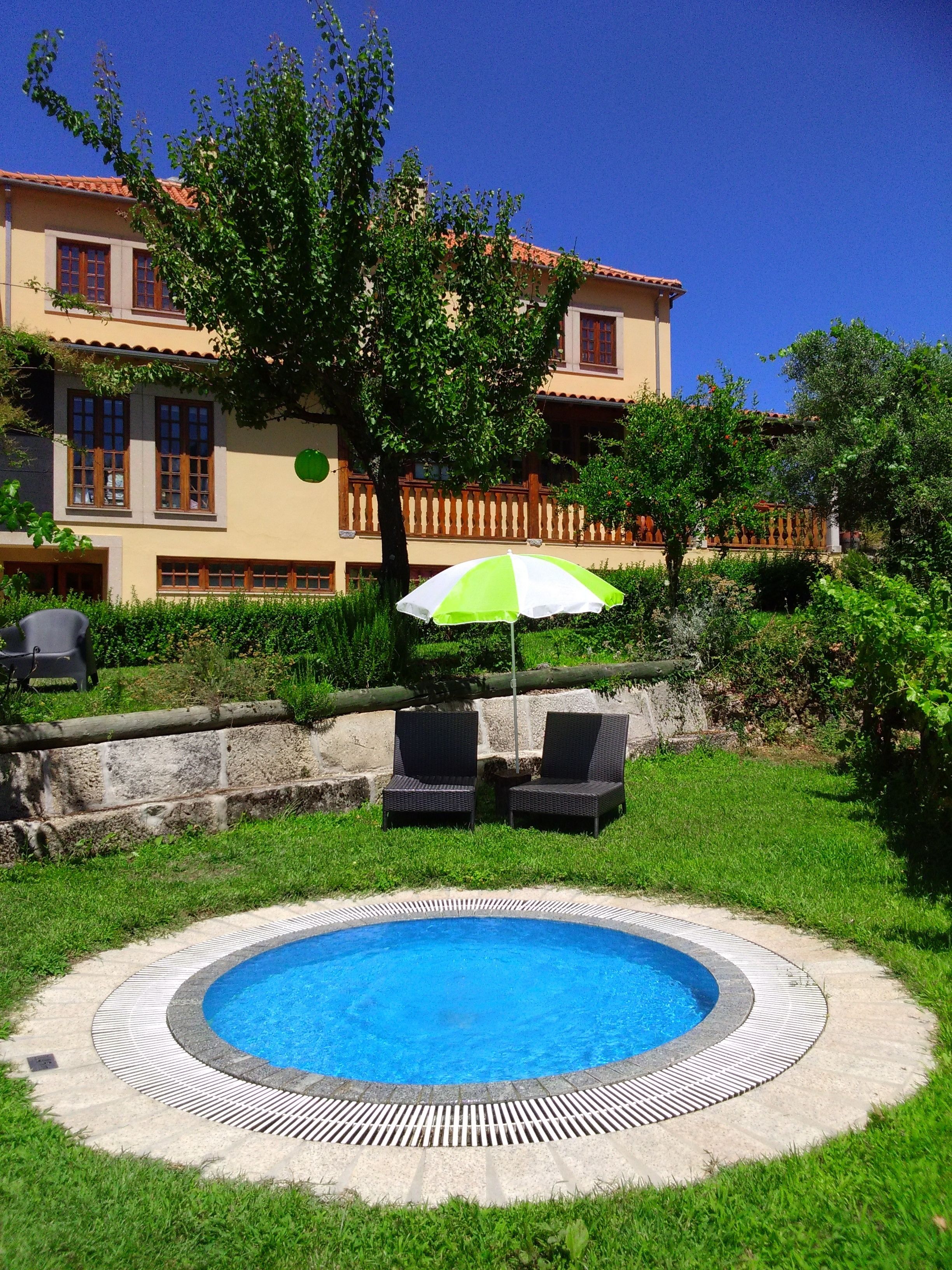 Uma piscina com um deck ao redor, duas espreguiçadeiras e um guarda-sol verde e branco.