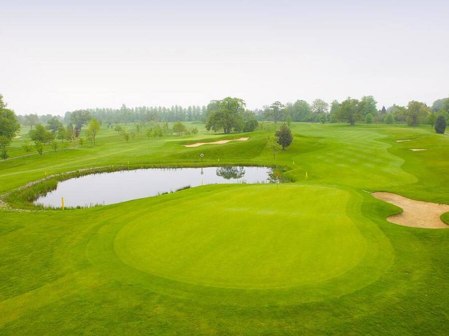 Um campo de golfe com lago, bunkers de areia e um green bem cuidado.