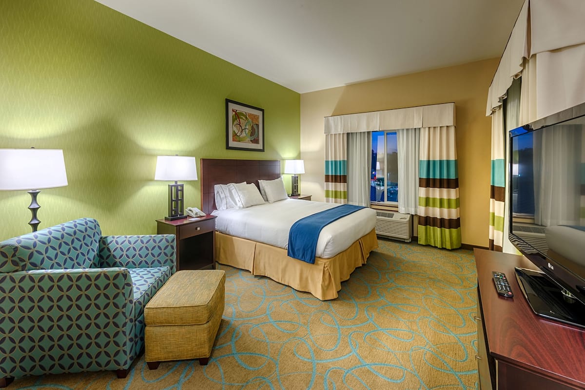 Quarto de hotel com cama, sofá, televisão e escrivaninha.