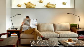 Uma sala de estar moderna com um sofá, uma mesa de centro e uma pessoa lendo um jornal.