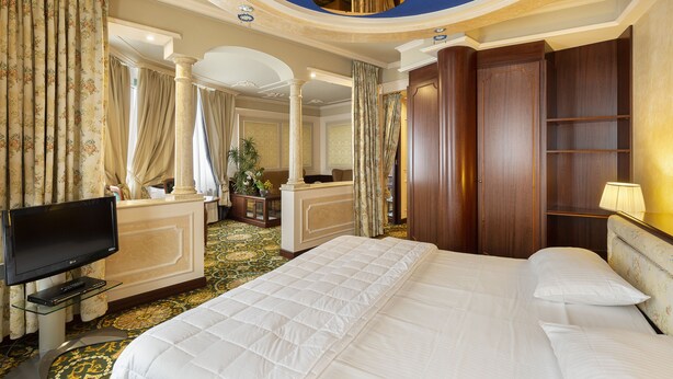 Quarto de hotel com uma cama grande, televisão, escrivaninha e espelho.
