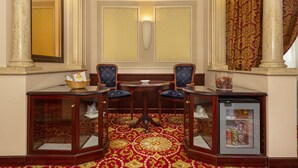 Quarto de hotel com área de refeições, incluindo uma mesa, duas cadeiras, um refrigerador e um tapete decorativo.