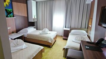 Quarto de hotel com duas camas, uma escrivaninha, uma cadeira, televisão e uma janela grande com cortinas.