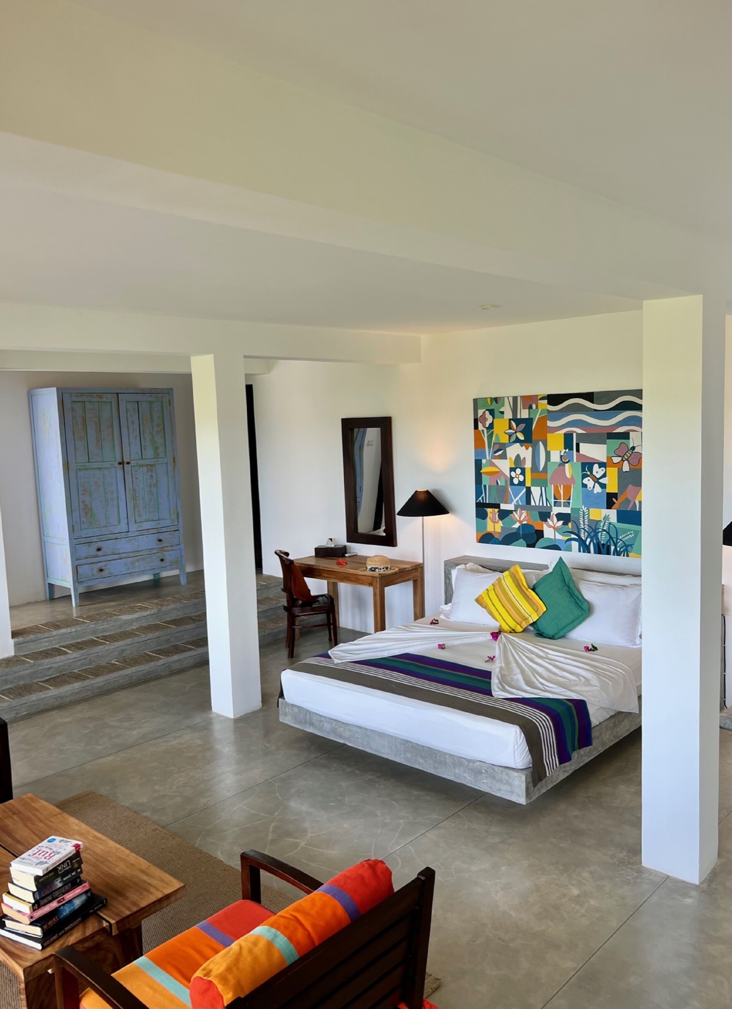 Quarto com cama, escrivaninha e cadeira. Há um quadro na parede e um guarda-roupa.