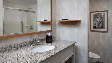 Casa de banho com bancada de granito, lavatório branco, espelho, sanita e um quadro emoldurado na parede.