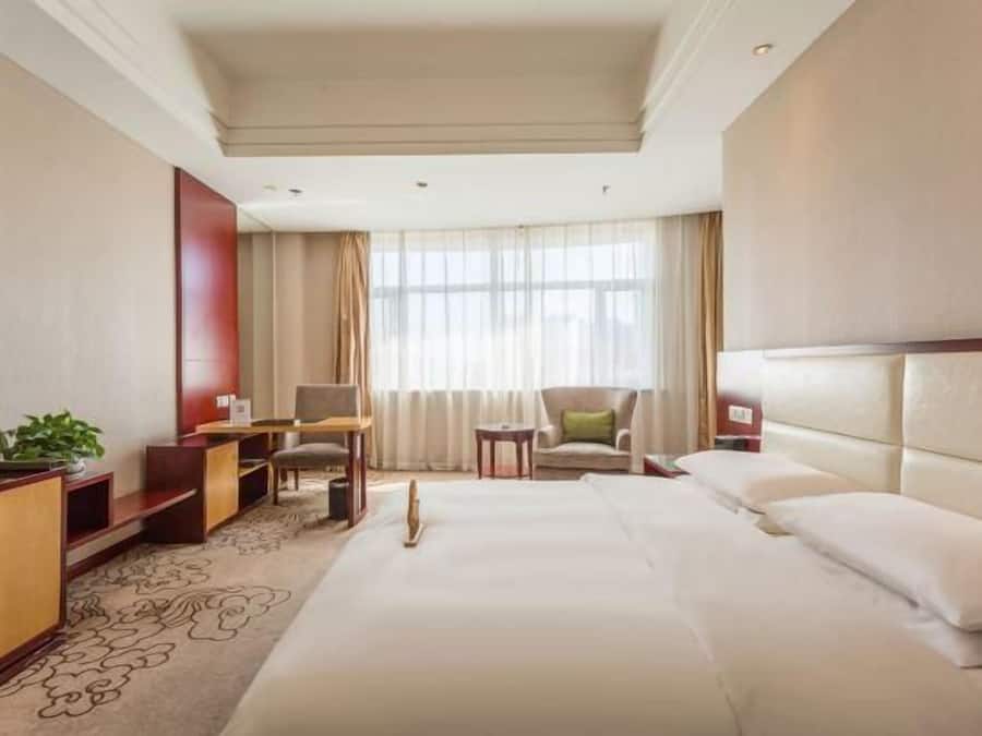 Quarto de hotel com cama grande, escrivaninha, cadeira, mesa pequena e televisão.
