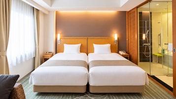 Quarto de hotel com duas camas, chuveiro em vidro e mesa de cabeceira com telefone.