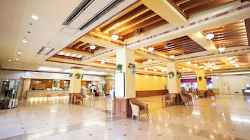 Um hall amplo com balcão de recepção, áreas de estar e teto alto com vigas de madeira e iluminação embutida.