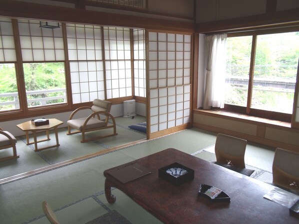 Um quarto japonês tradicional com piso de tatame, uma mesa baixa, uma cadeira acolchoada e portas corrediças shoji.