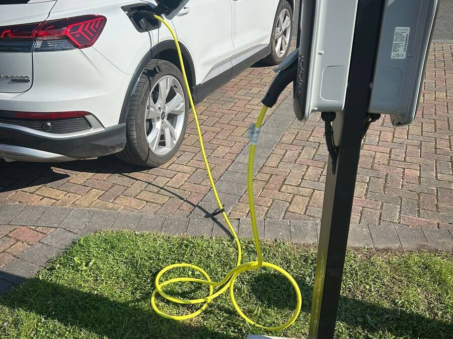 Um carro branco estacionado ao lado de uma estação de carregamento com um cabo amarelo conectado.