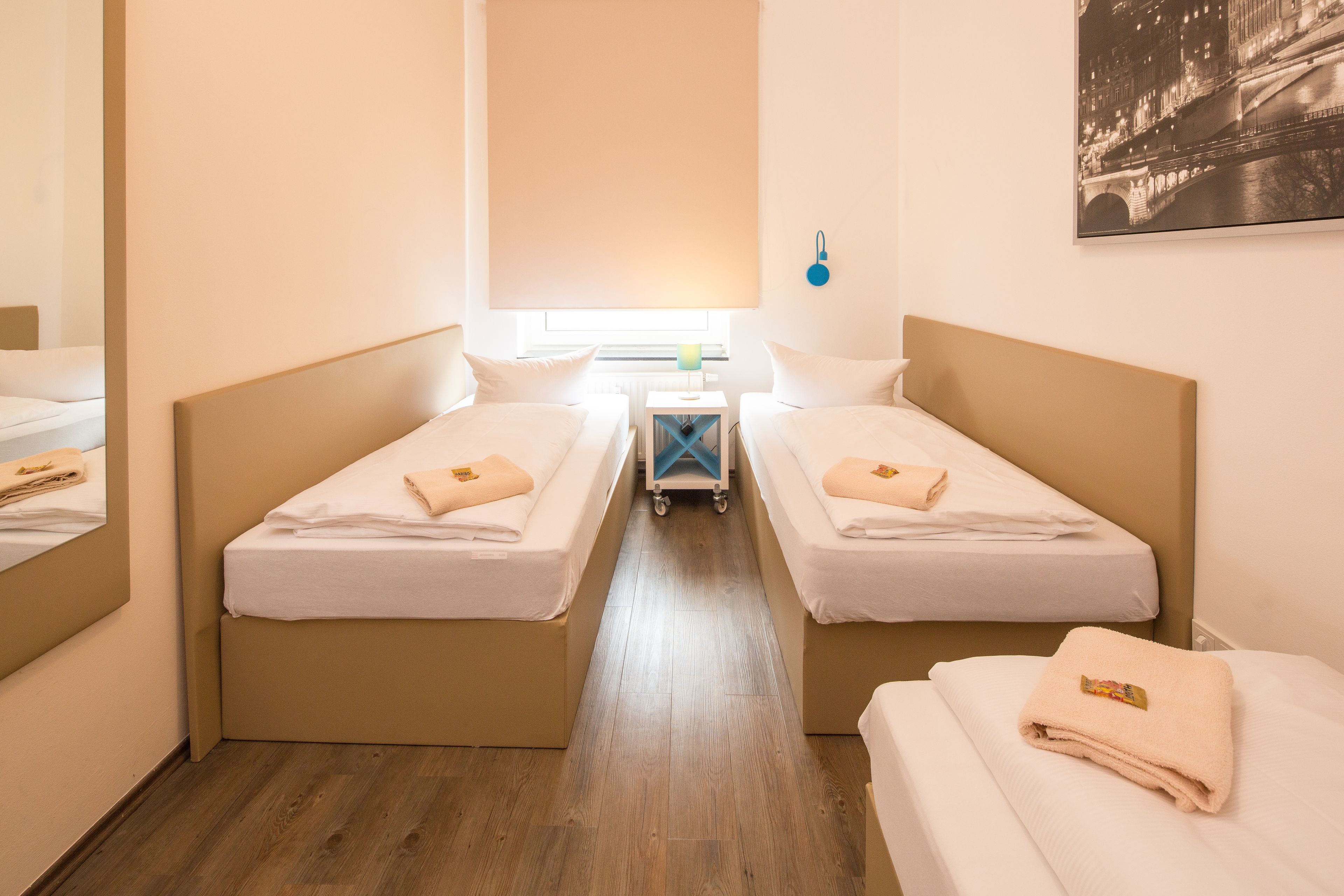 Quarto de hotel com duas camas de solteiro, uma mesa pequena com abajur e janela com vista para uma ponte.