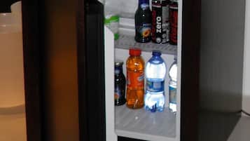 Uma pequena geladeira com diversas bebidas, incluindo refrigerantes e água.