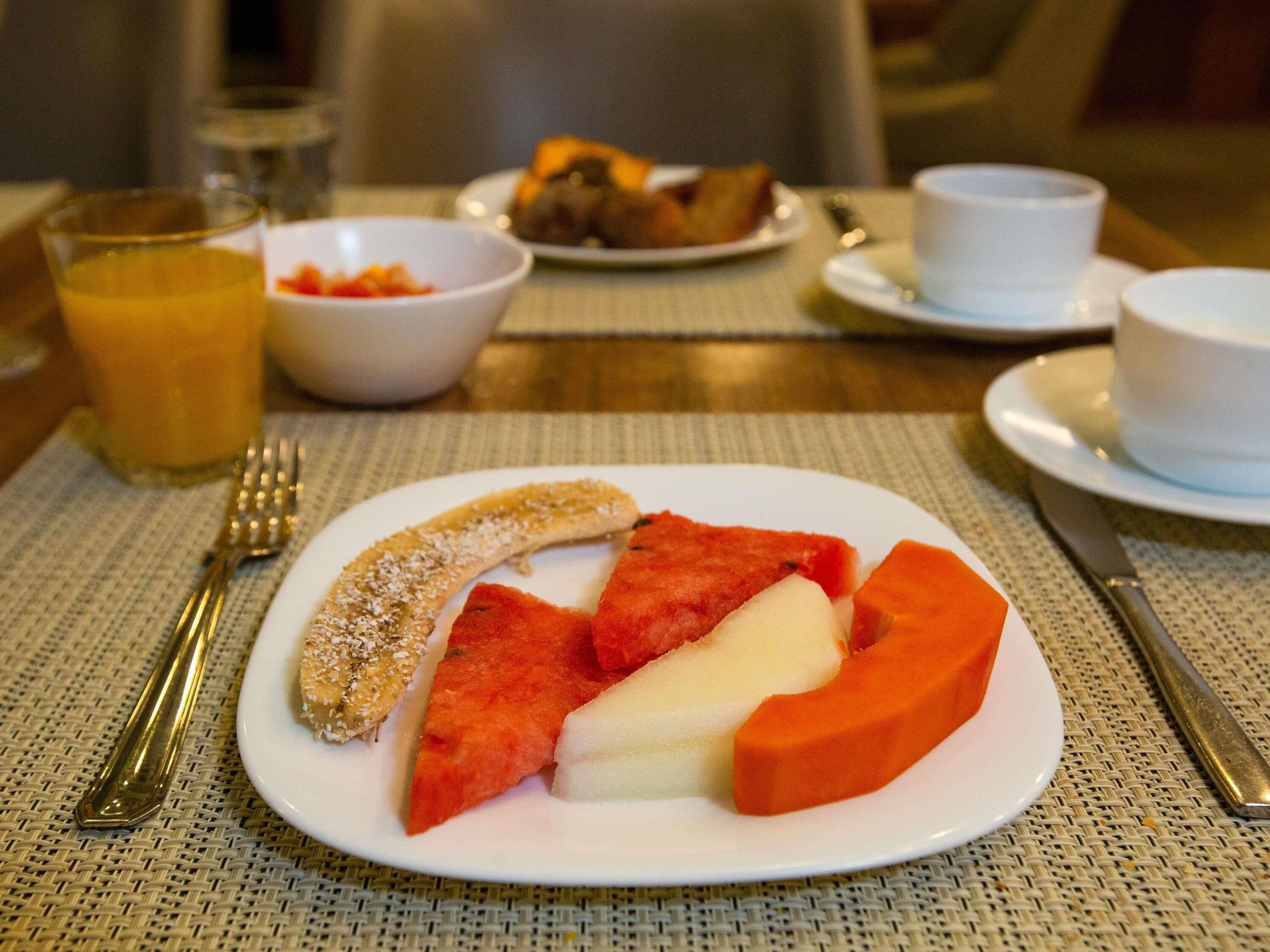 Prato de café da manhã com banana, morangos e uma fatia de queijo sobre um descanso de tecido trançado.