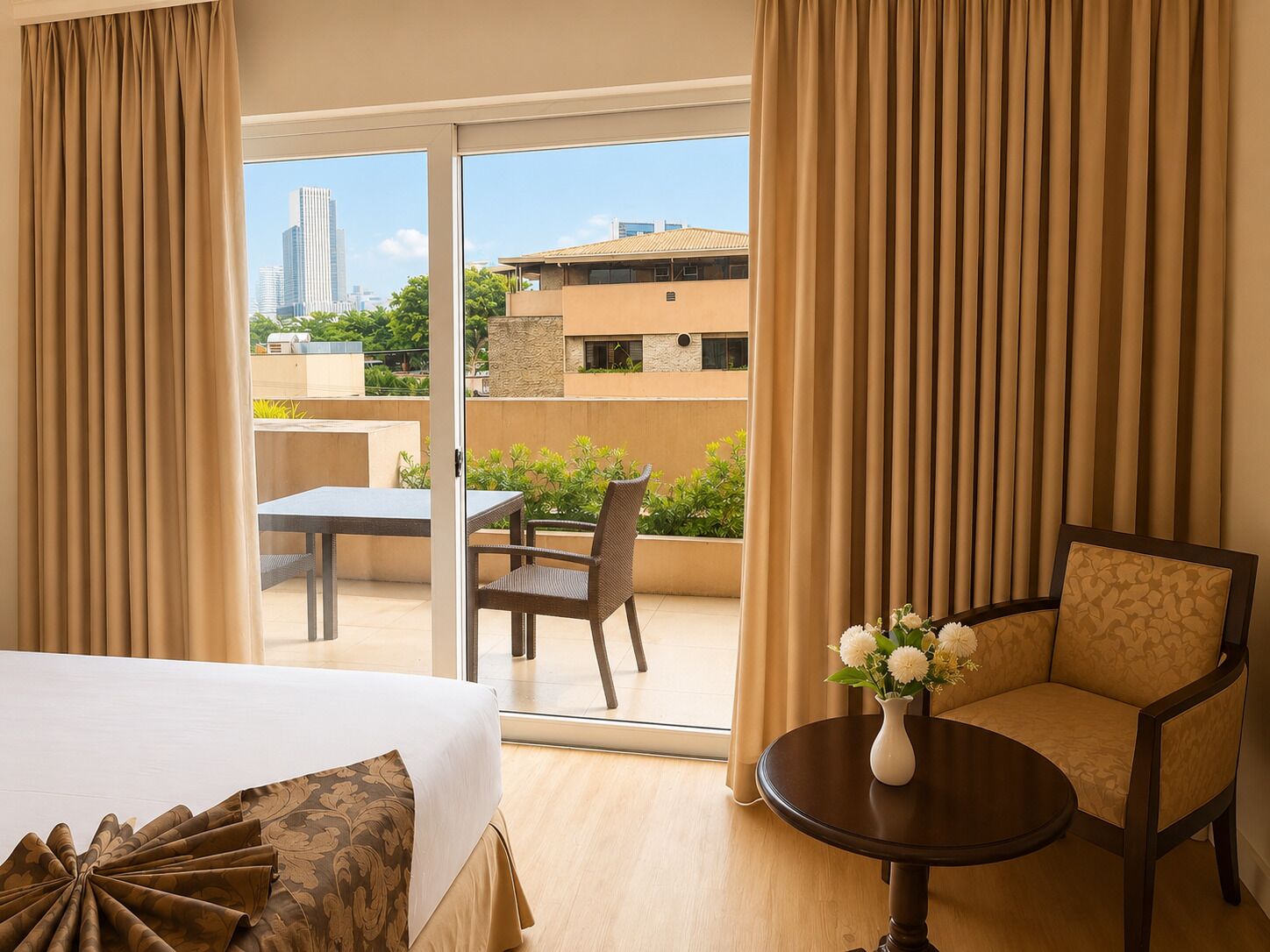 Quarto de hotel com cama, mesa com um vaso de flores, cadeira e varanda com mesa e cadeira.