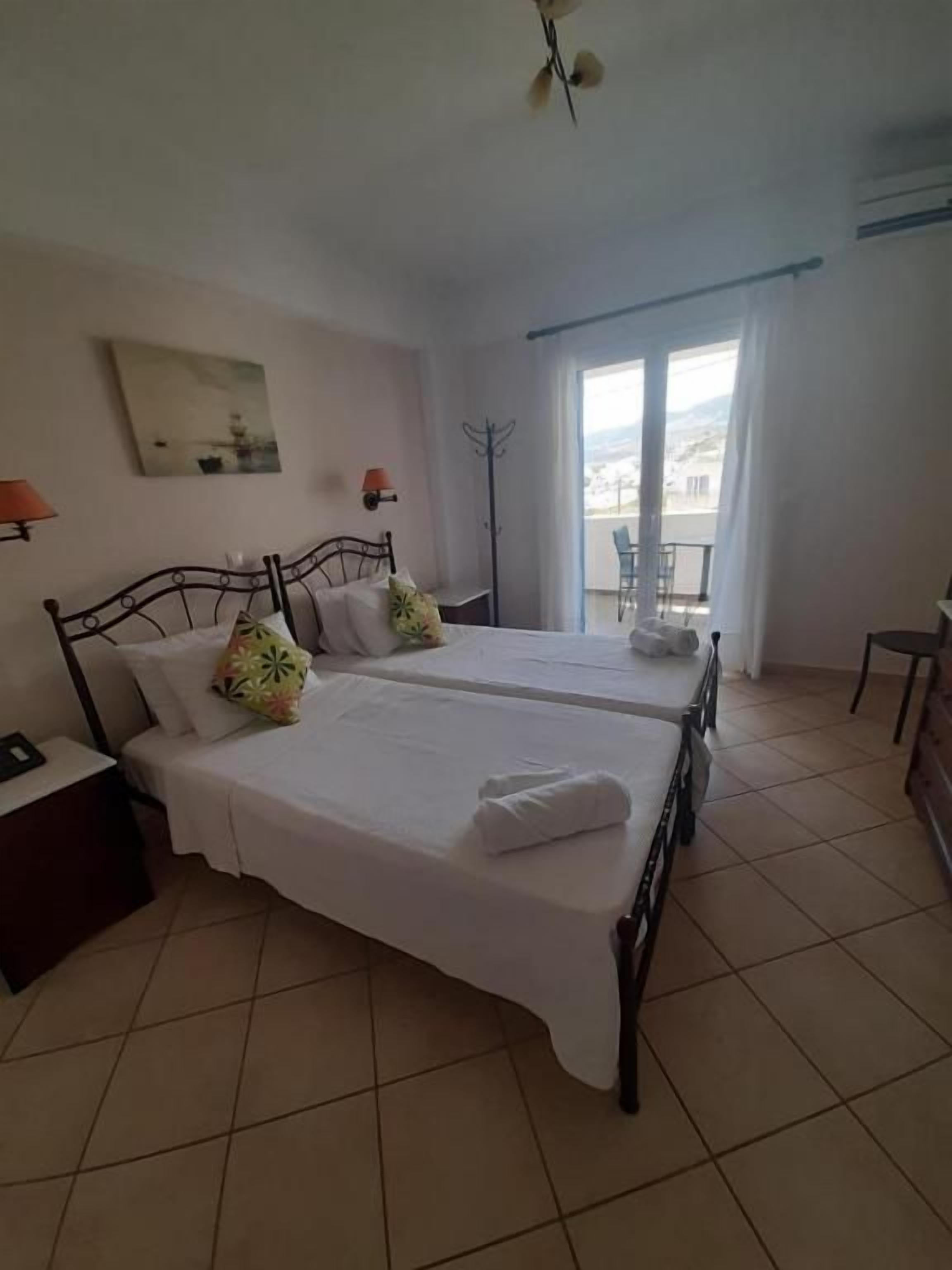 Quarto de hotel com duas camas, varanda e vista para o mar.