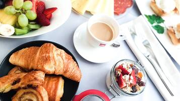 Um café da manhã com croissants, queijo, frutas e uma xícara de café.