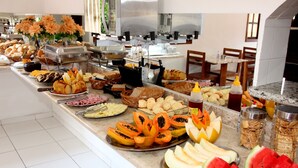Buffet com diversos alimentos, incluindo frutas, pães e doces.