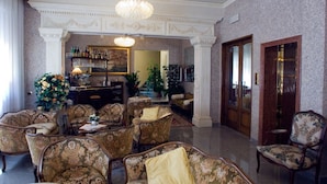 Uma área de estar formal com móveis ornamentados, um bar com parede espelhada e um candelabro.