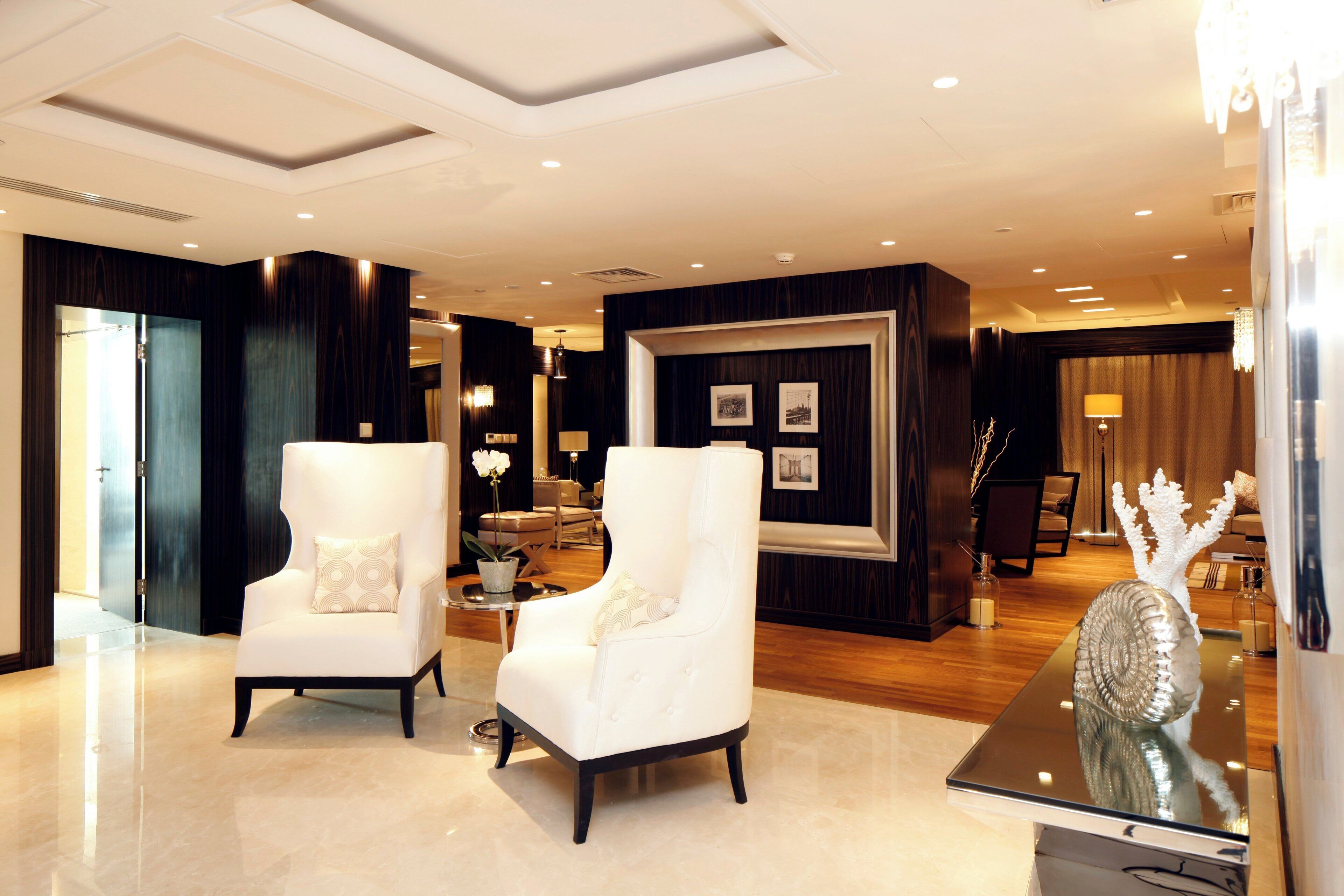 Um saguão moderno de hotel com dois poltronas brancas, uma mesa de centro de vidro e uma escultura decorativa.