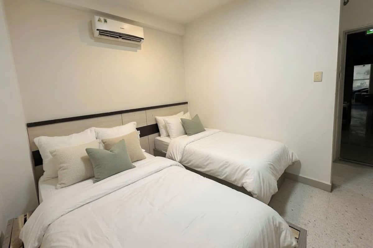 Quarto com duas camas, ar condicionado fixado na parede e porta que dá para outra área.