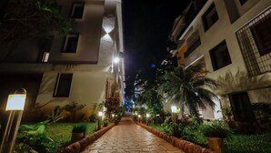 Uma passagem noturna ladeada por edifícios com janelas iluminadas e plantas em vasos.