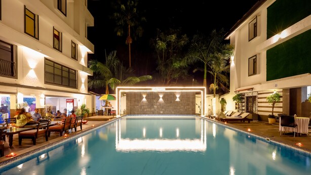 Uma piscina com deck azulejado, rodeada por áreas de estar ao ar livre e palmeiras.